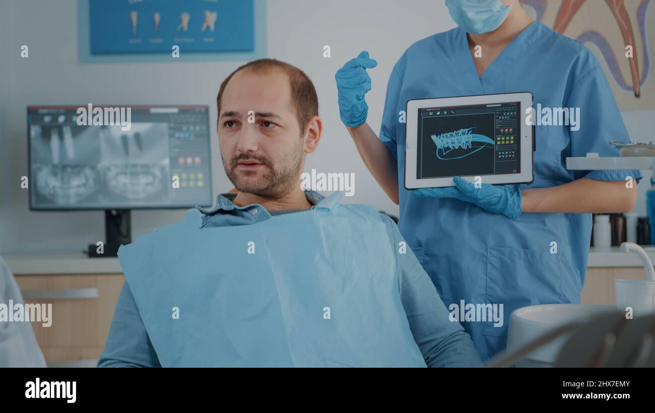 Dentistry assistant showing x ray scan results on tablet to patient ...