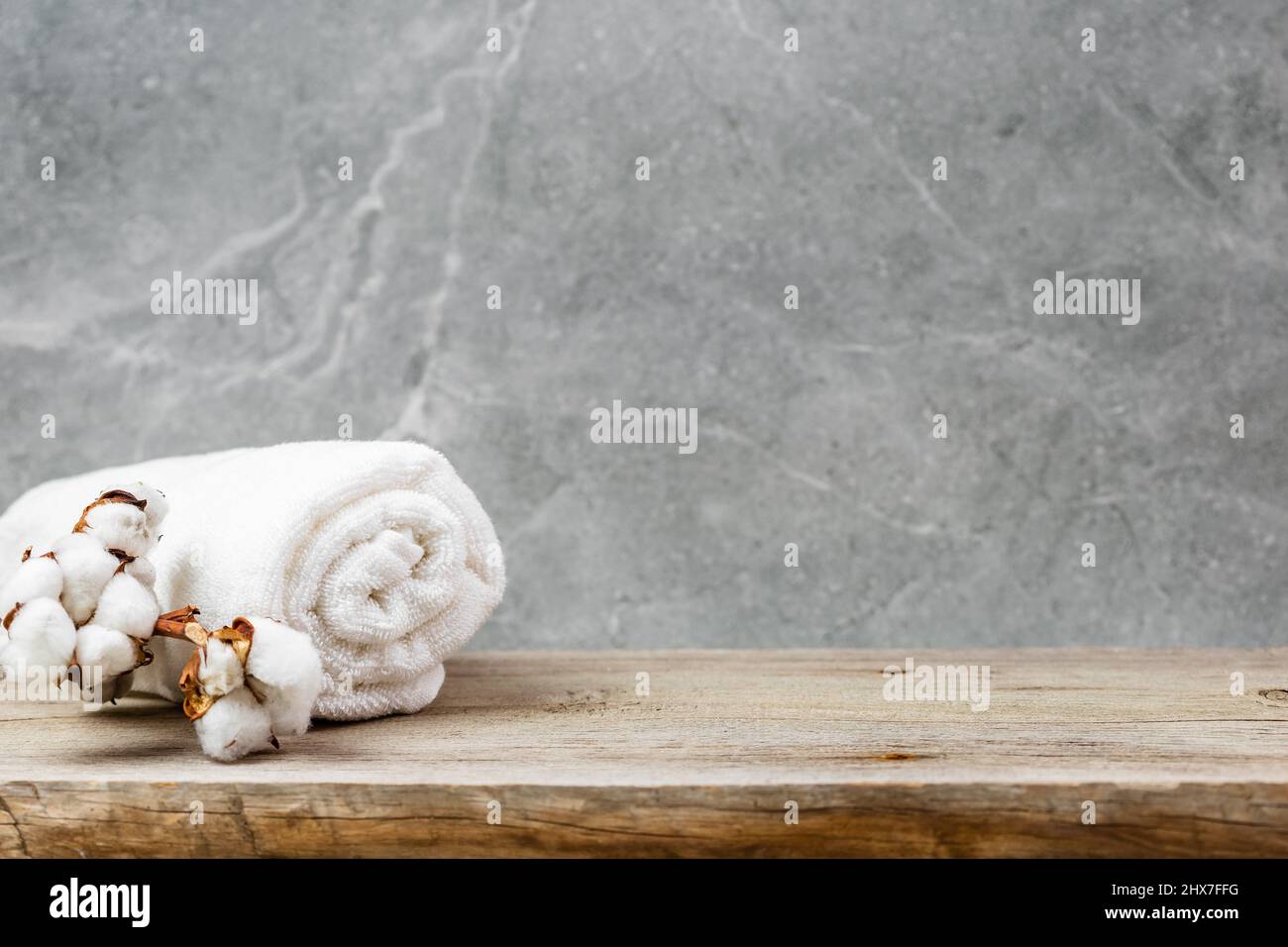 White cotton towel rolled up and cotton plant flower branch over grey ...