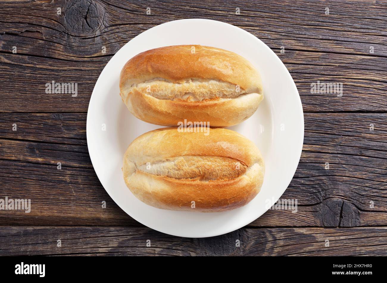 Loaves of small white bread in plate on old wooden table, top view ...