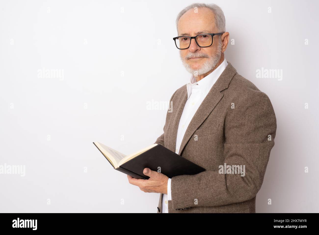Portrait of senior man in elegant clothing reading a book standing ...