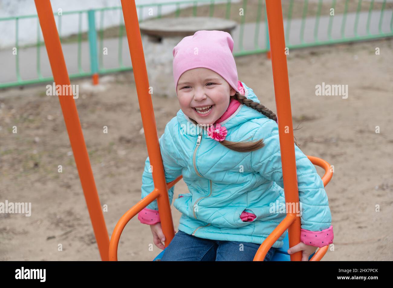 A child in a blue jacket swings on a swing. Happy five-year-old girl with pigtails having fun on ...