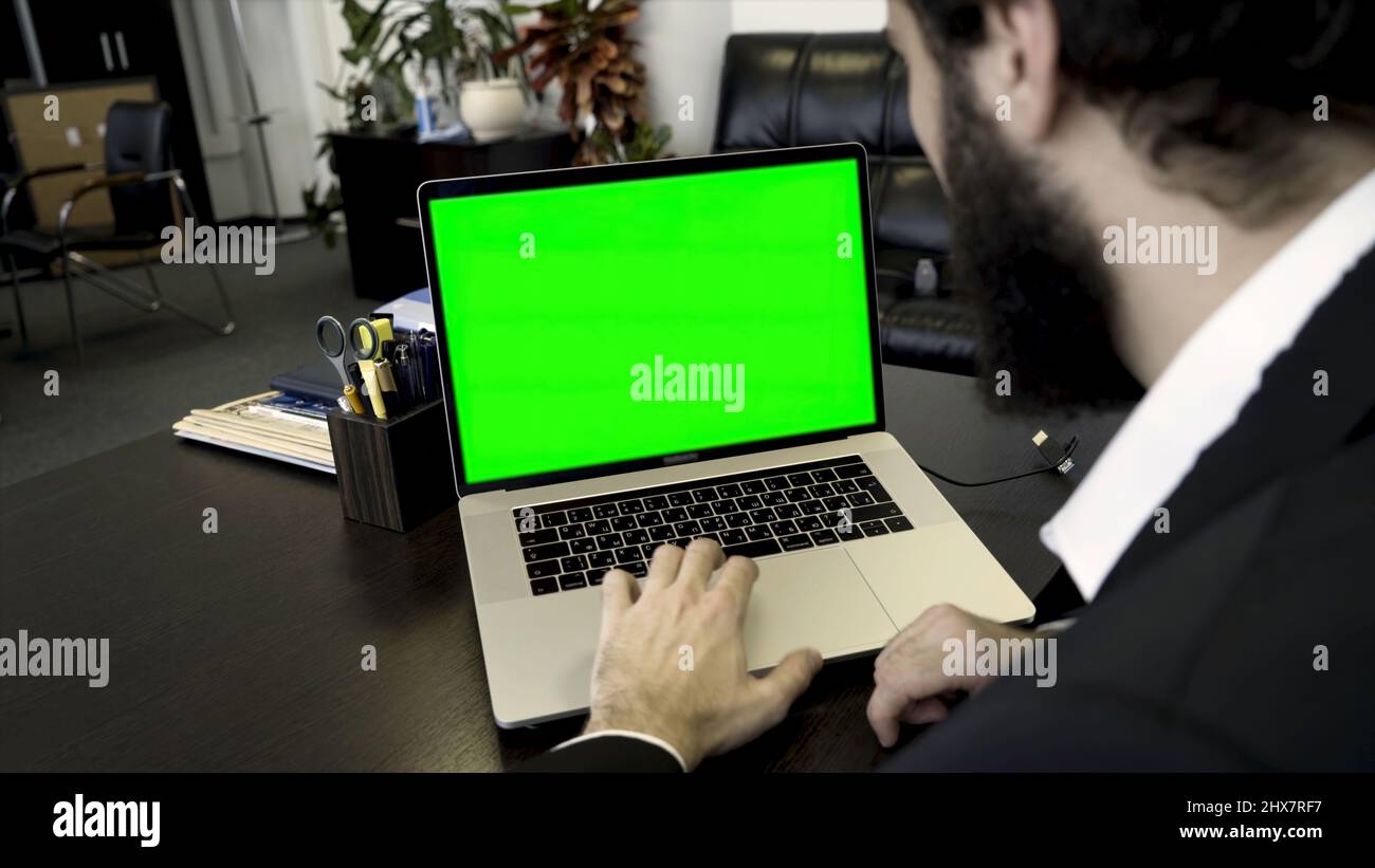 Close up for a bearded man typing on a computer laptop with a green ...