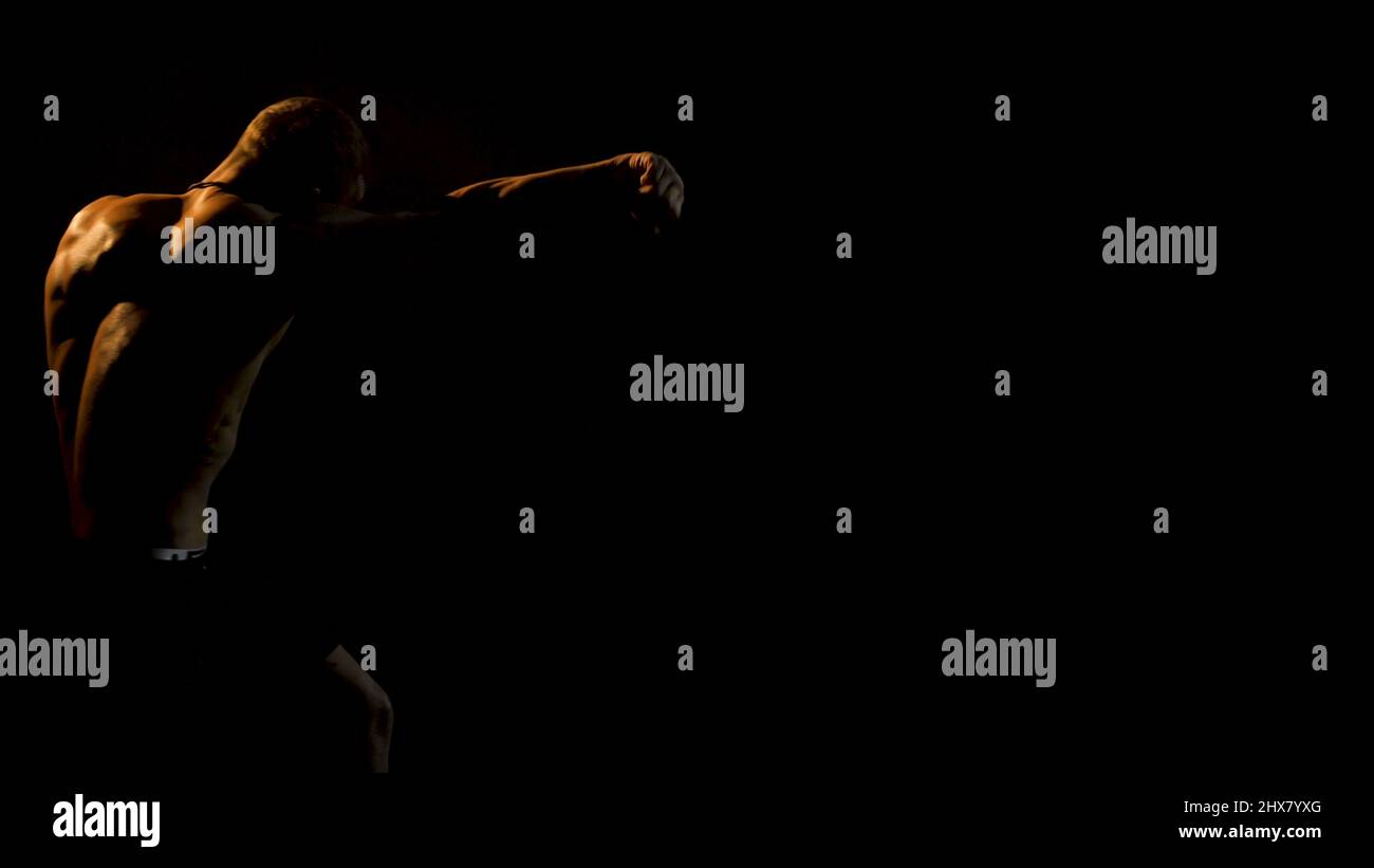 Boxer doing shadow Boxing in a dark room. Man of athletic build makes a ...