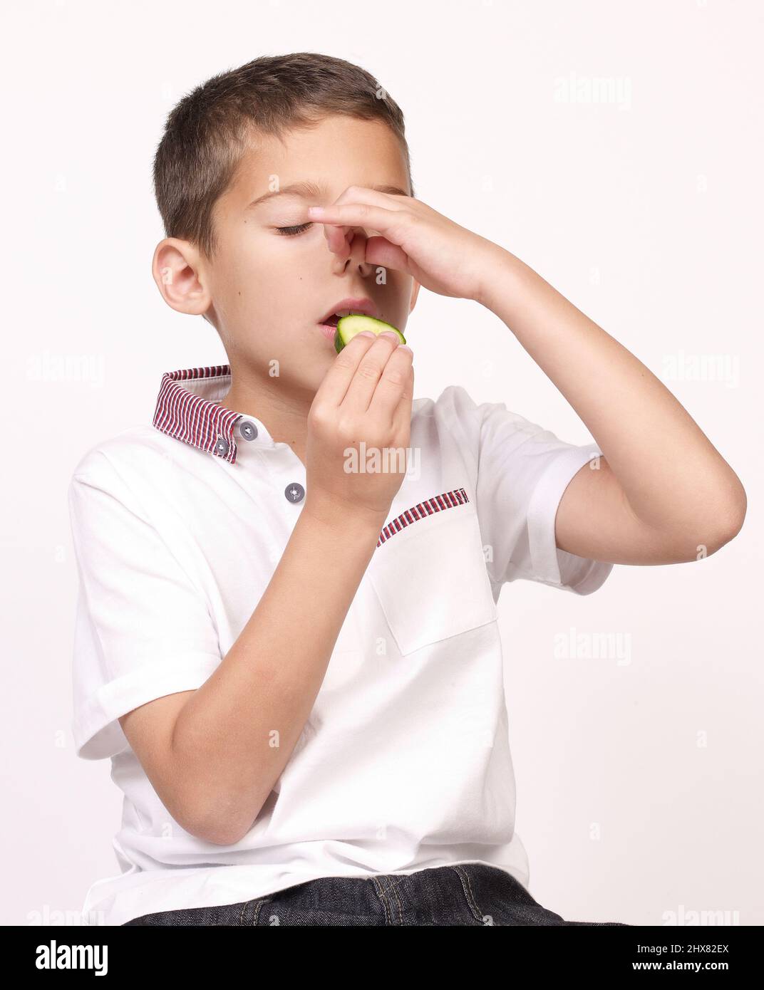 Boy holding the top of his nose as he holds a slice of cucumber to his ...