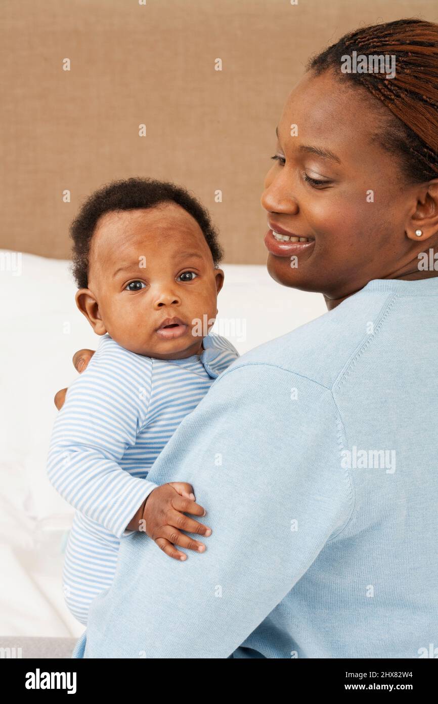 Side view of mother holding baby boy against one shoulder, baby looking ...