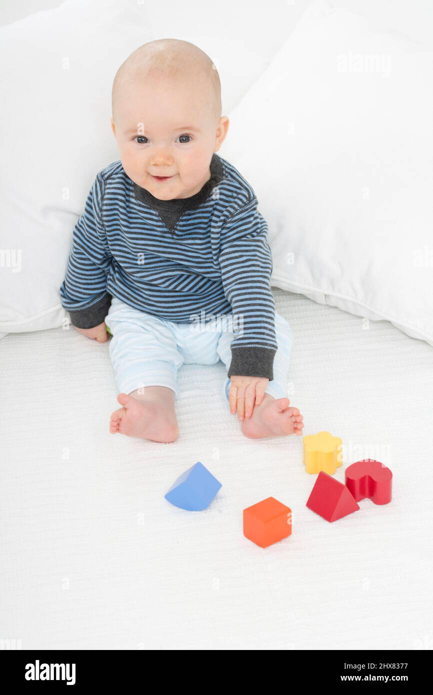 Baby boy sitting on carpet propped up by cushions with plastic block ...
