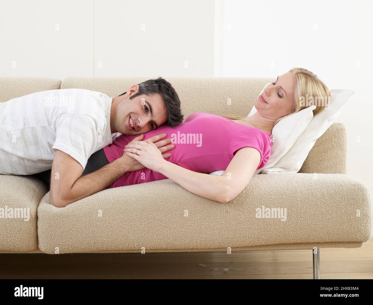 Pregnant woman lying on sofa as her partner lies with his head on her ...