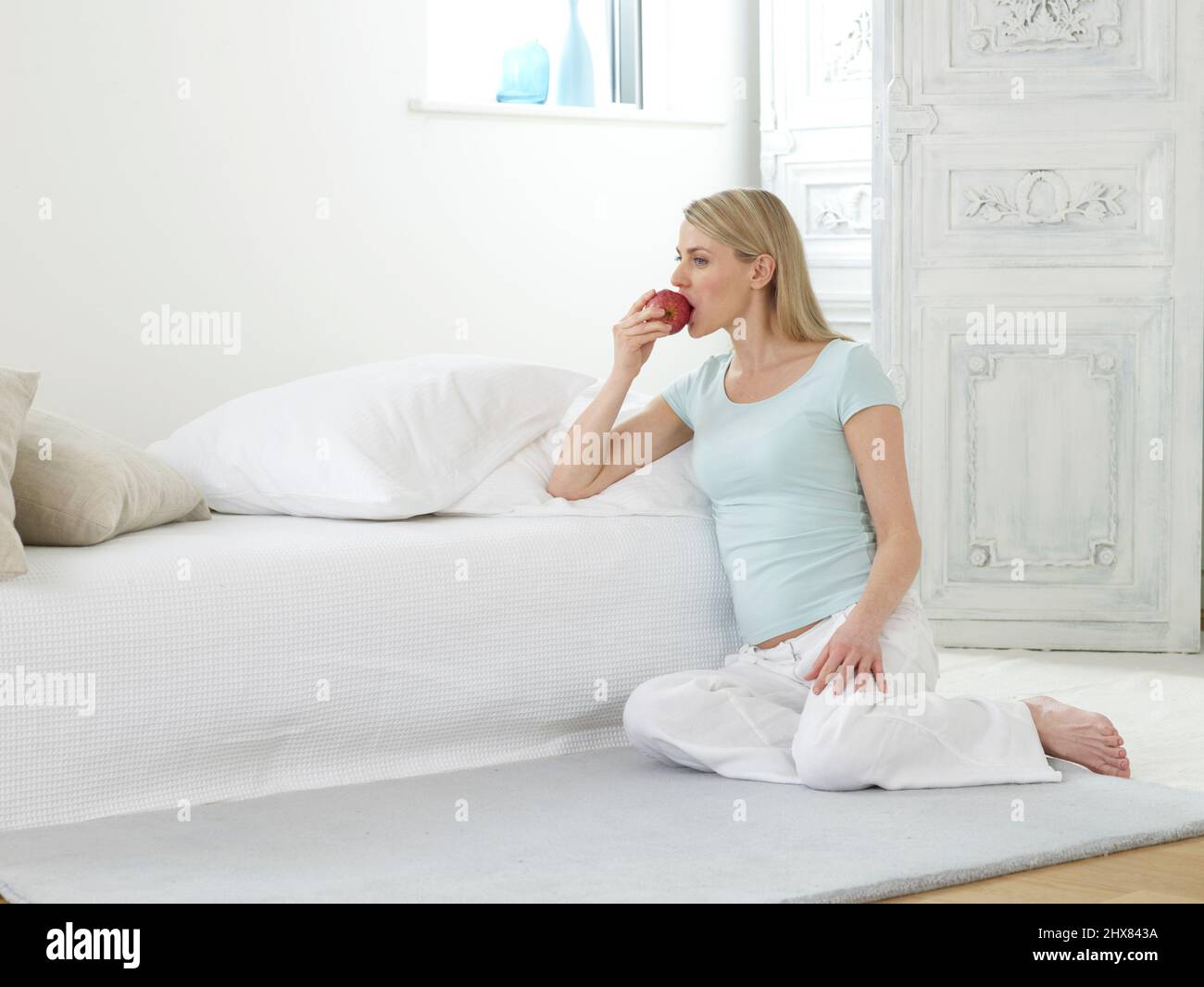 Pregnant woman sitting on floor leaning against bed and eating an apple ...
