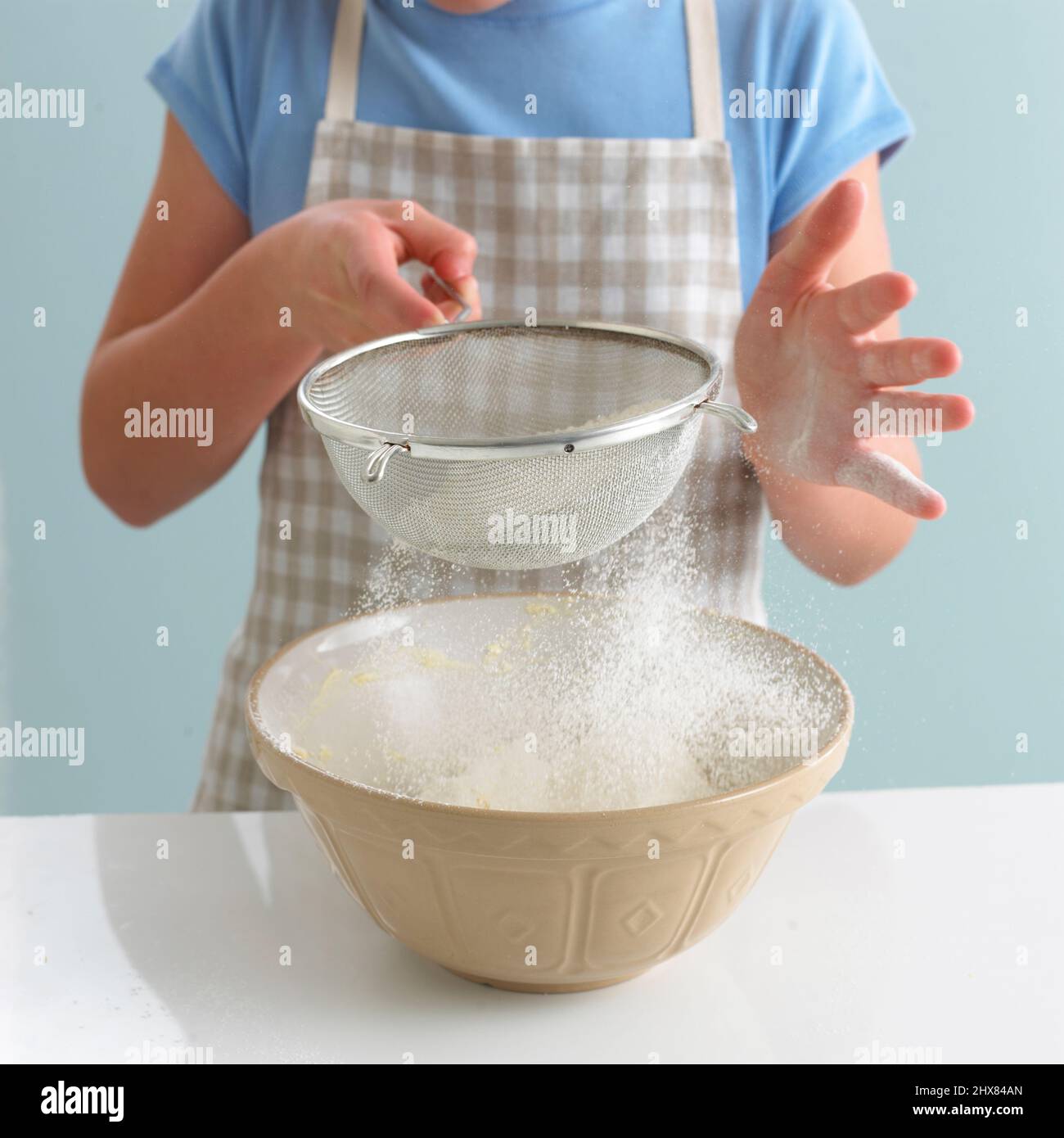 Girl sieving flour into large mixing bowl, front view Stock Photo - Alamy