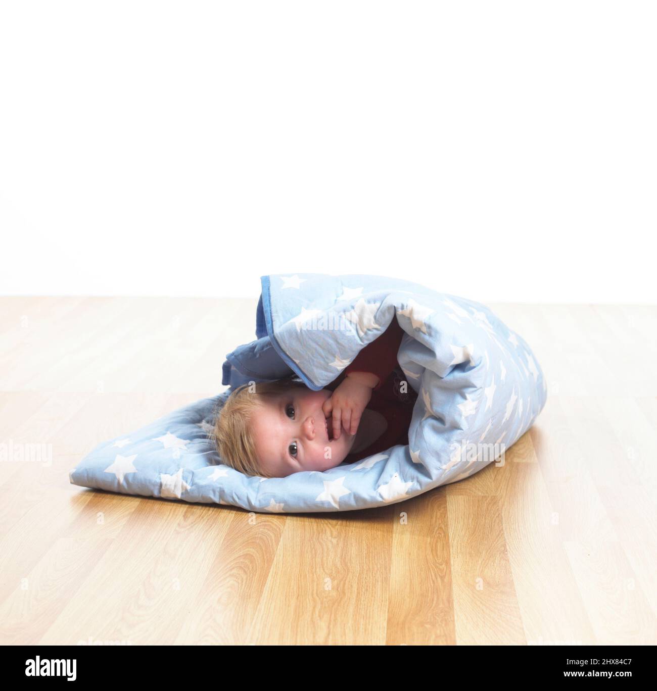 Toddler hiding in duvet on wooden floor Stock Photo - Alamy