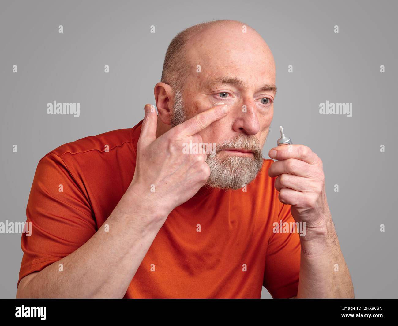 senior man is applying a retinol cream under his eyes, skincare and ...