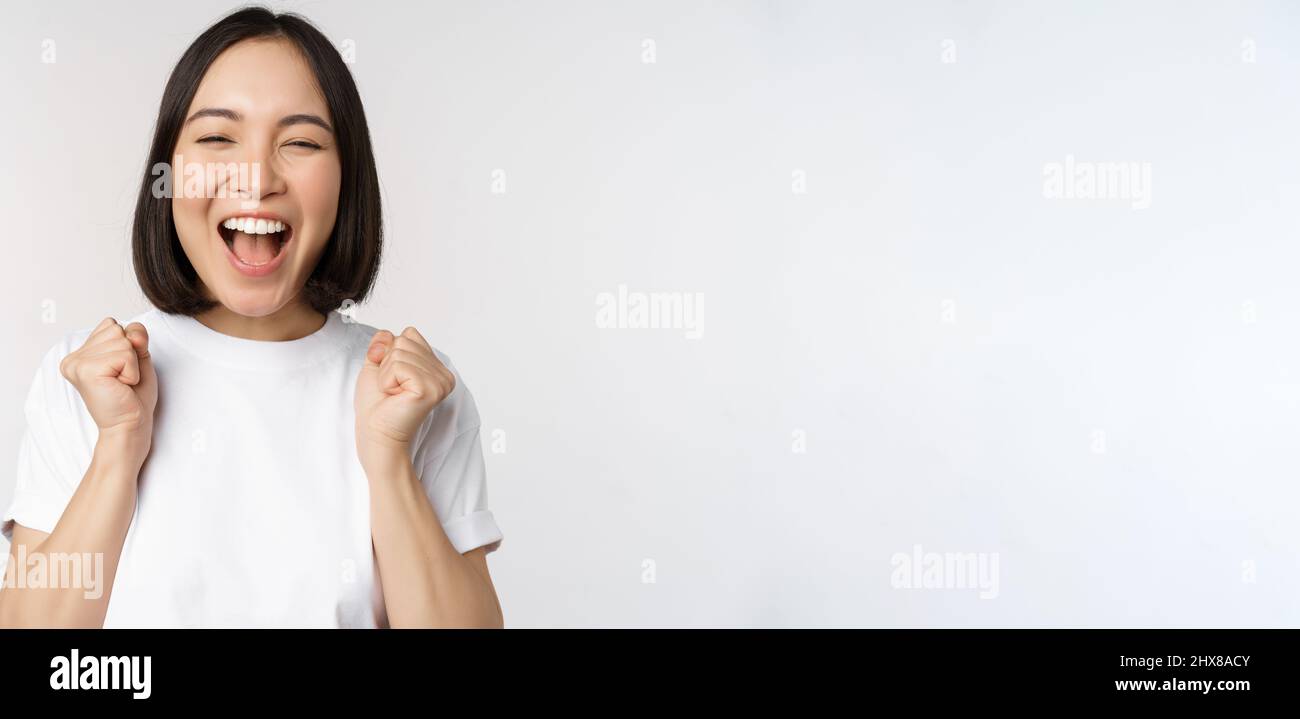 Portrait of enthusiastic asian woman winning, celebrating and ...