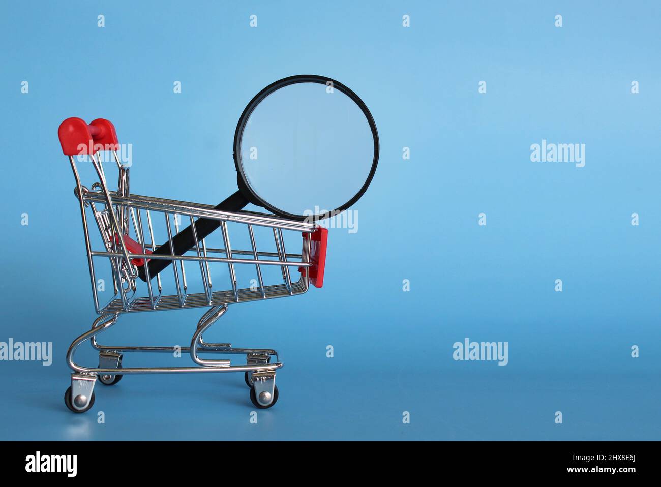 Magnifying glass inside shopping cart. Blue background. Product search ...