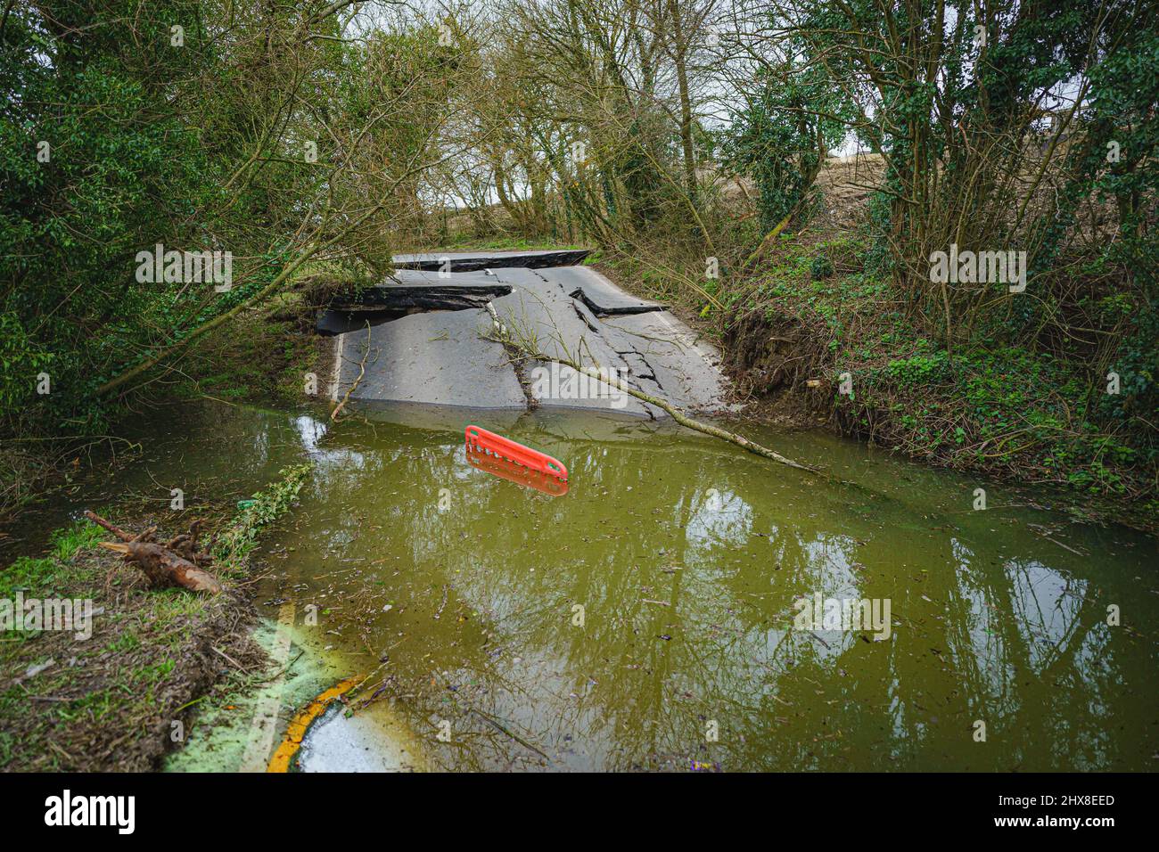 A flood in the base of a sunken road amid broken tarmac on a section of ...