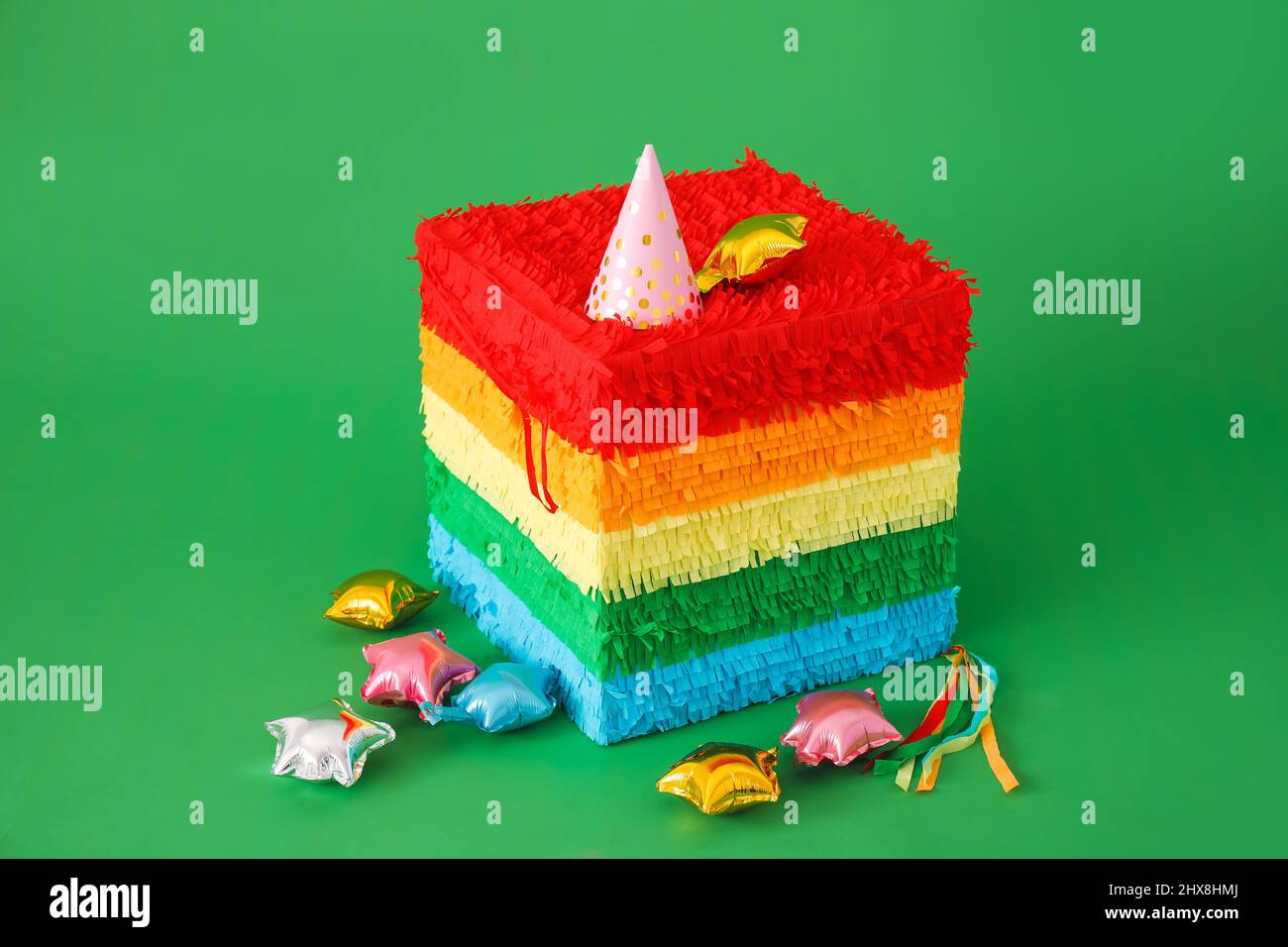 Mexican pinata in shape of cube with party hat and balloons on green ...