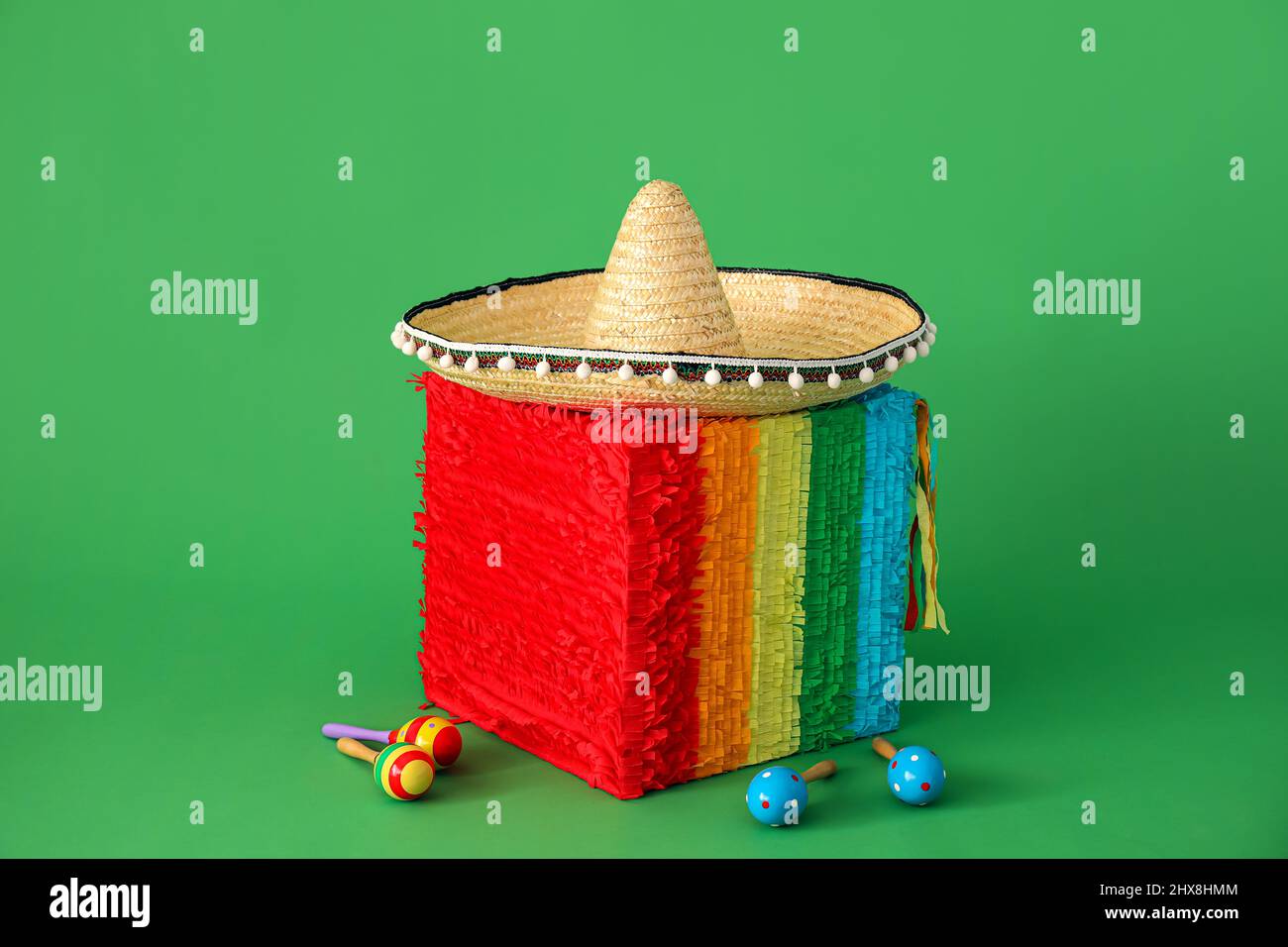 Mexican pinata in shape of cube with sombrero hat and maracas on green ...