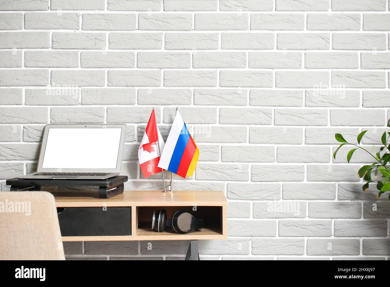 Workplace with laptop, flags of Canada and Russia near grey brick wall ...