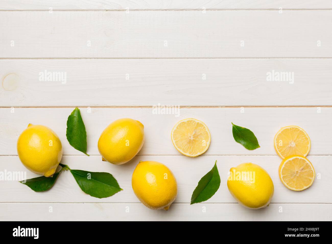 Many fresh ripe lemons with green leaves on colored background, top ...