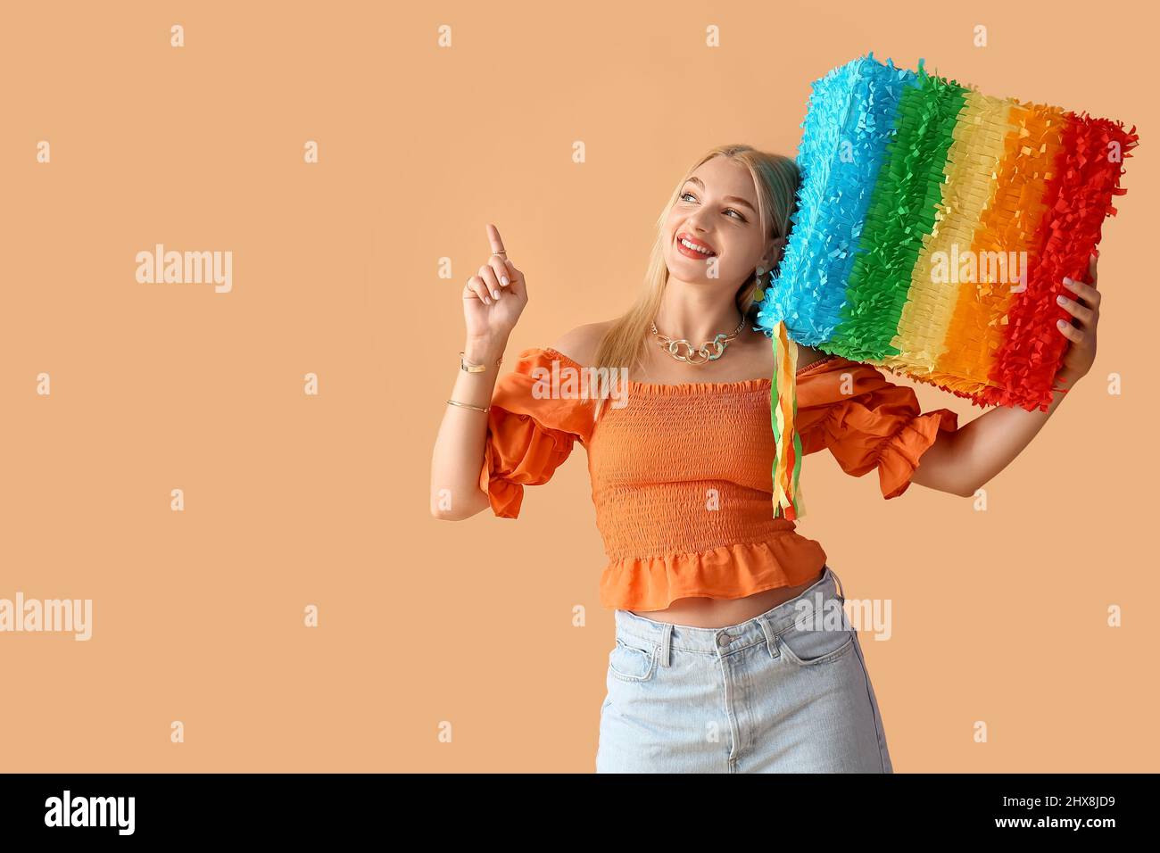 Young woman with Mexican pinata pointing at something on beige ...