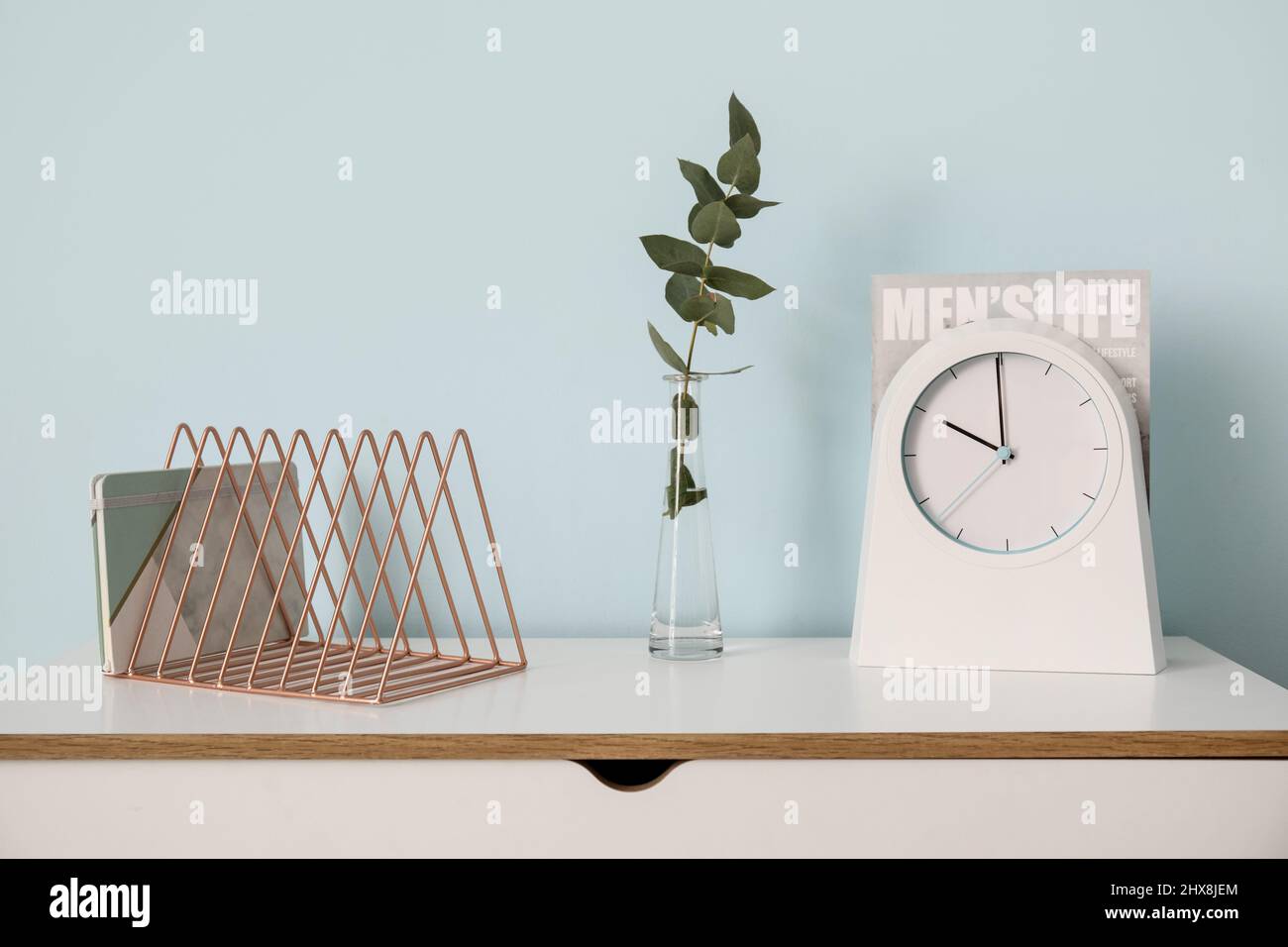Metal organizer with notebook, vase and clock on shelf near blue wall ...