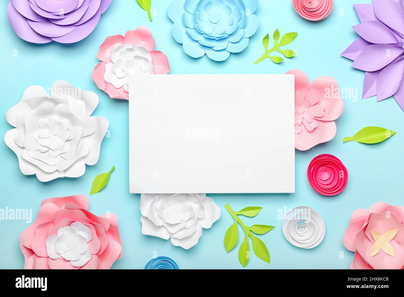 Beautiful handmade paper flowers and blank paper sheet on blue ...