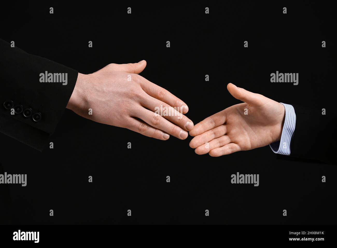 Business workers reaching out to handshake on black background, closeup ...