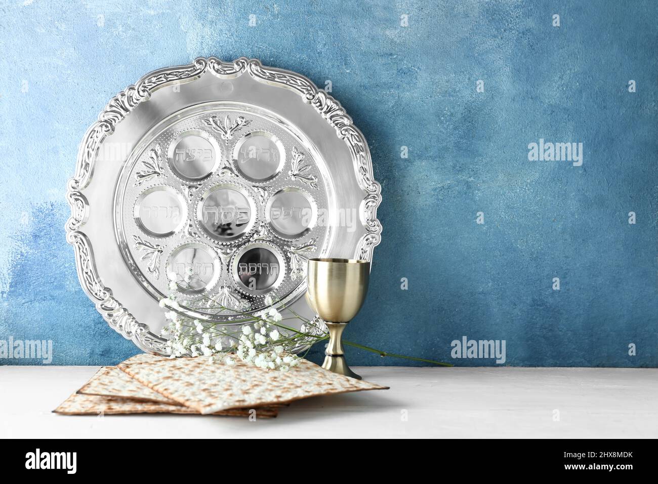 Passover Seder plate with cup of wine and matza on table against color ...