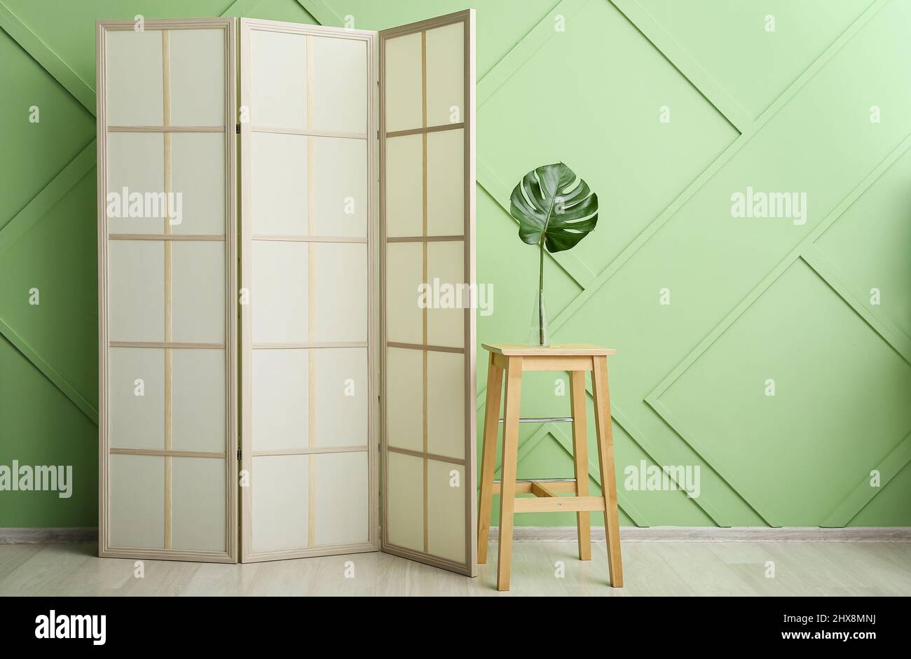Stylish folding screen and vase with monstera leaf on table near color ...