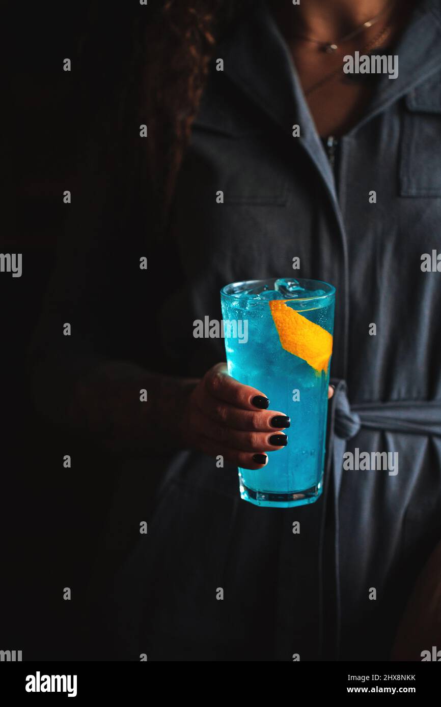 Woman holding blue cocktail in a highball with ice Stock Photo - Alamy