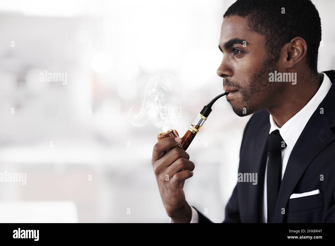 Vaping in style. A young businessman smoking an electronic pipe in an ...