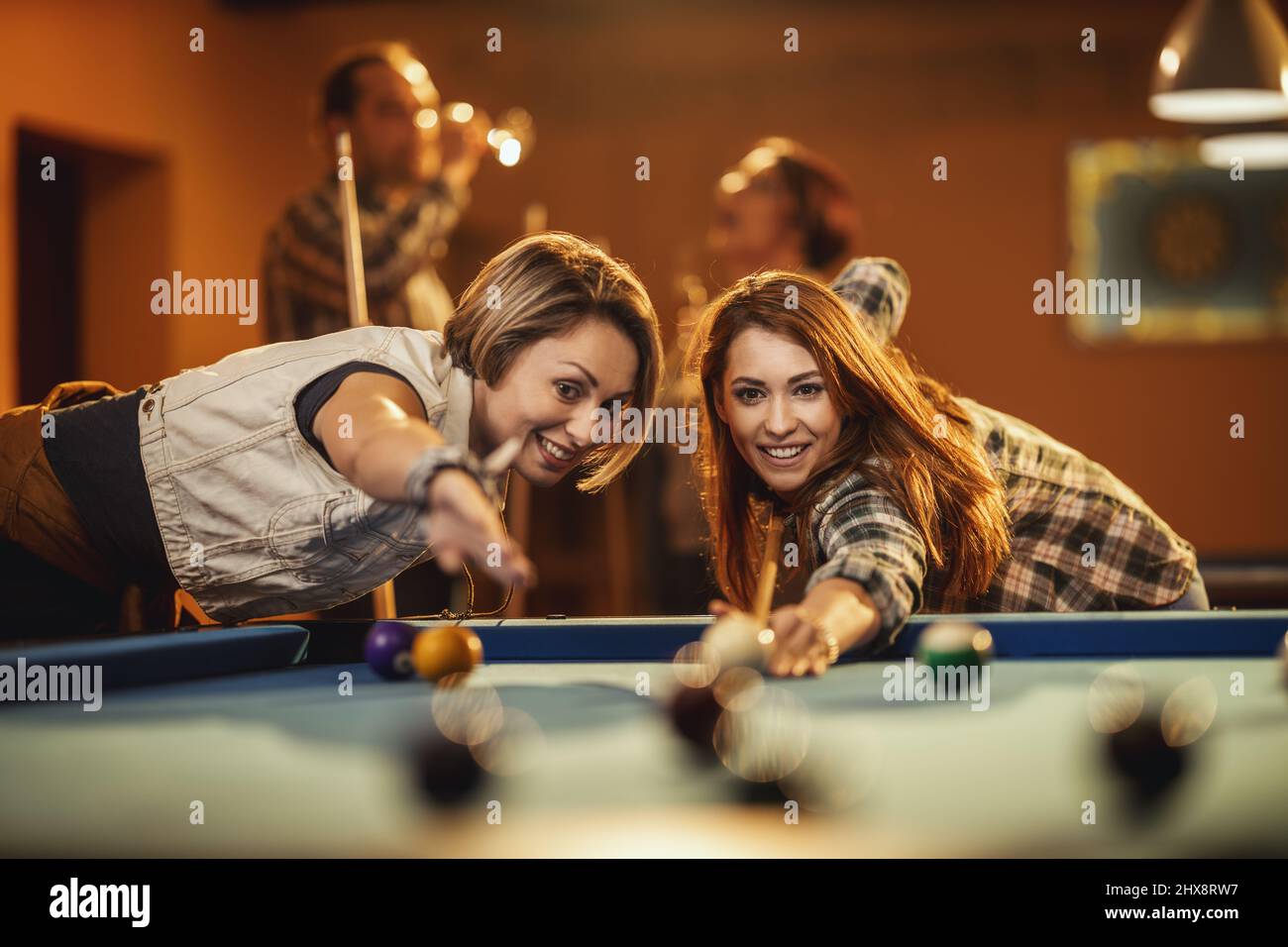 Young smiling cheerful friends are playing billiards in bar after work ...