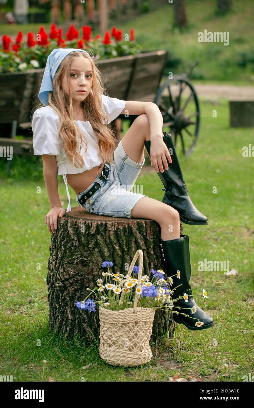 Tween girl sitting on stump on lawn in country estate with basket of ...