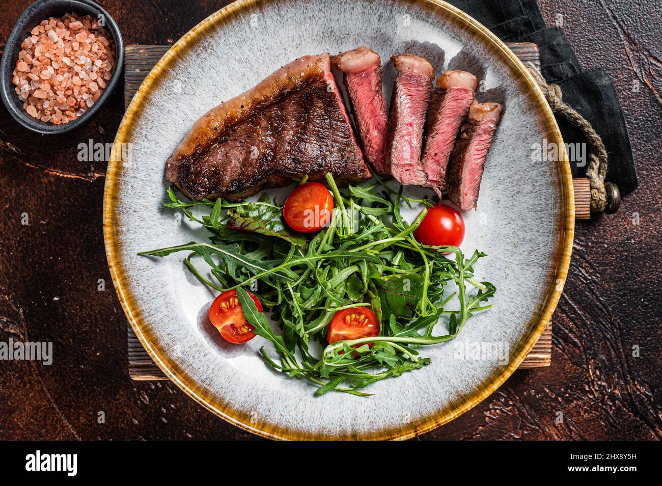 Grilled Top sirloin beef meat steak in plate with vegetable salad. Dark ...