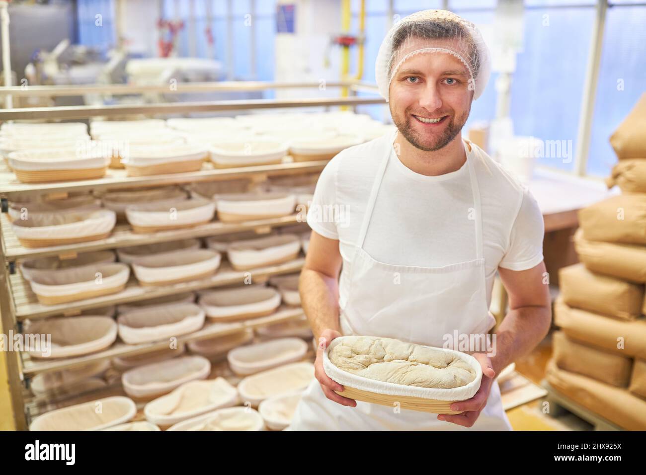 Smiling young man as a baker shows a loaf of bread in the bakery or ...