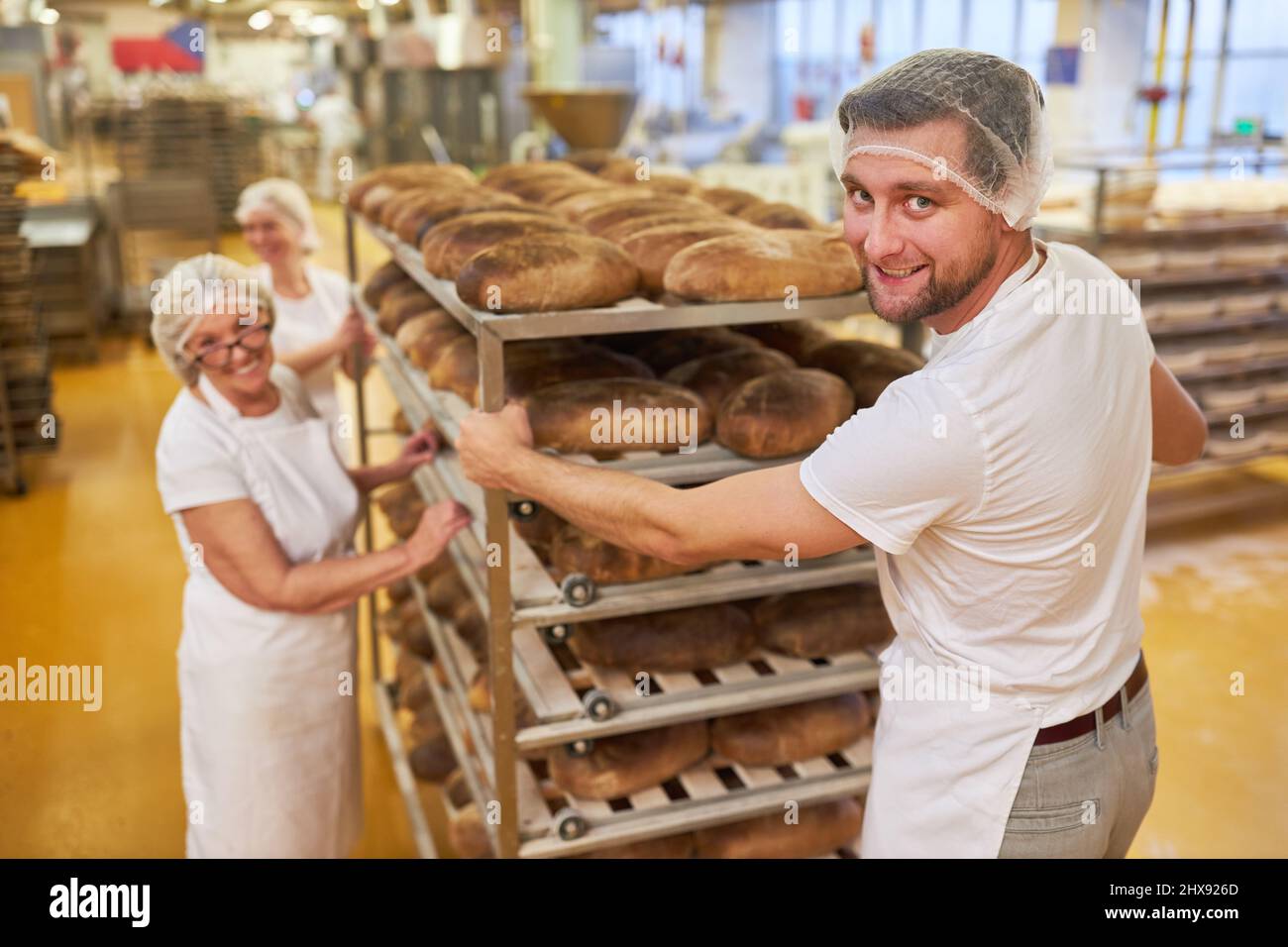 Baker team in the family bakery pushes a shelf trolley with fresh bread ...