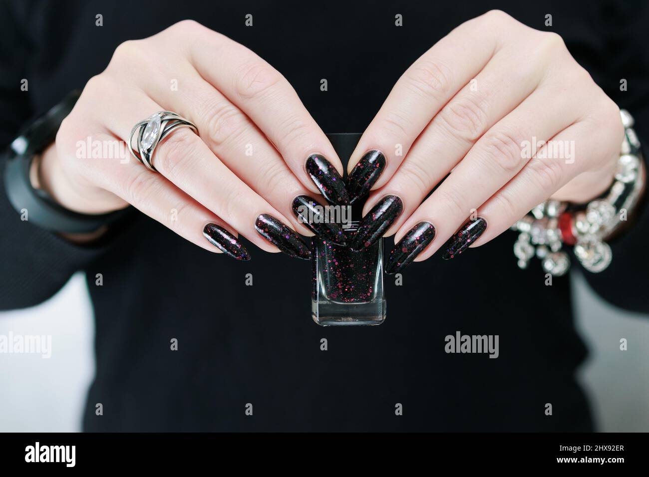 Female hands with long nails and total black manicure holding a bottle ...