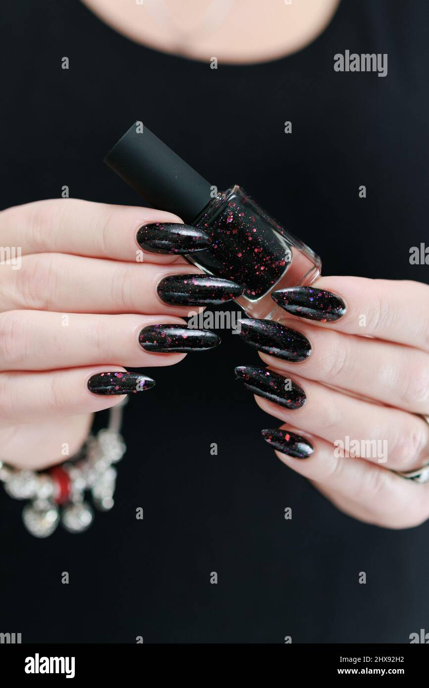 Female hands with long nails and total black manicure holding a bottle ...