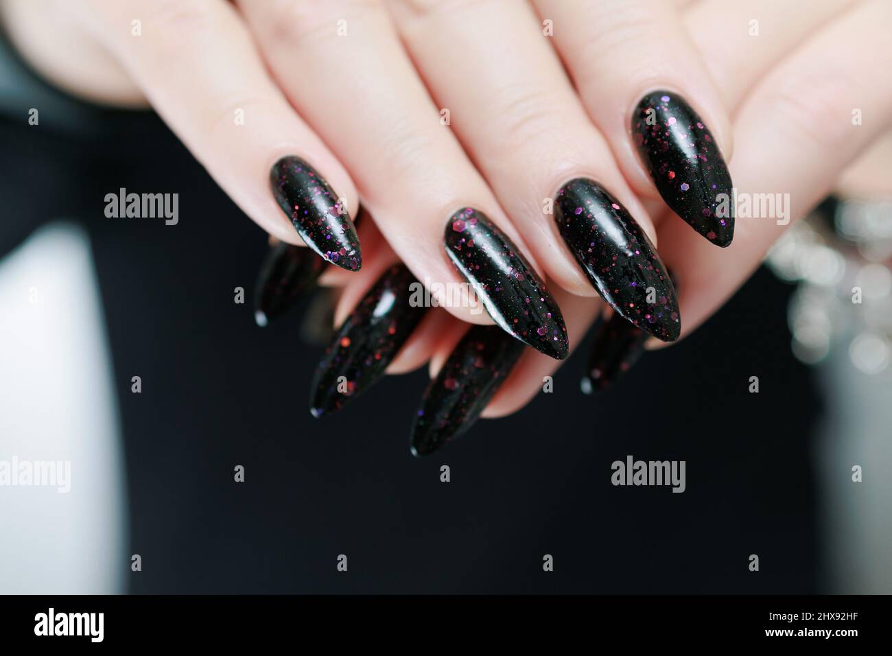 Female hands with long nails and total black manicure holding a bottle ...