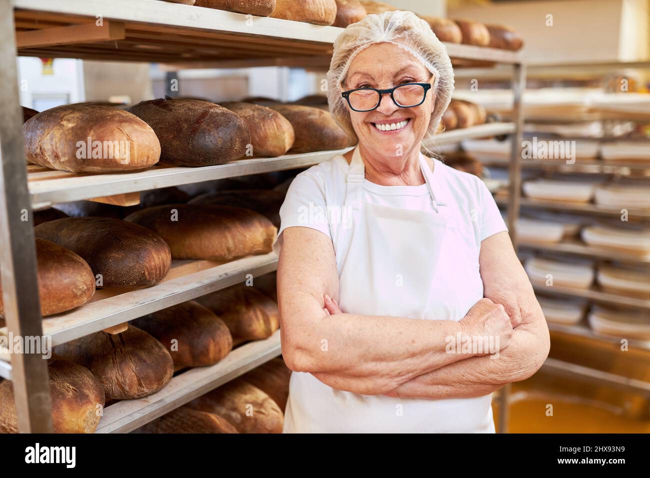 Happy senior woman as chef in her bakery in front of baked loaves with ...
