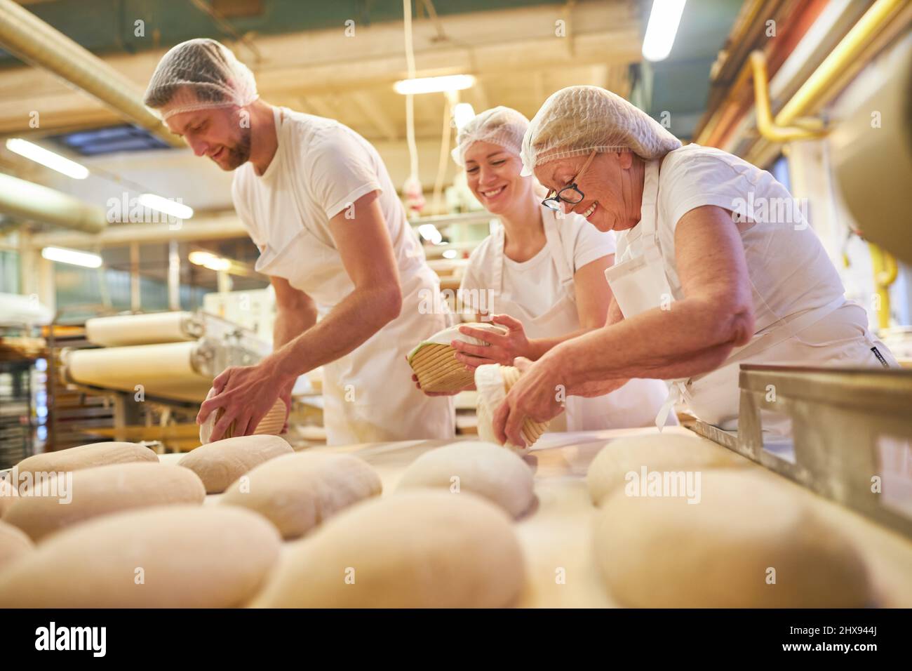 Senior woman as a baker with a team baking a loaf of bread in the ...