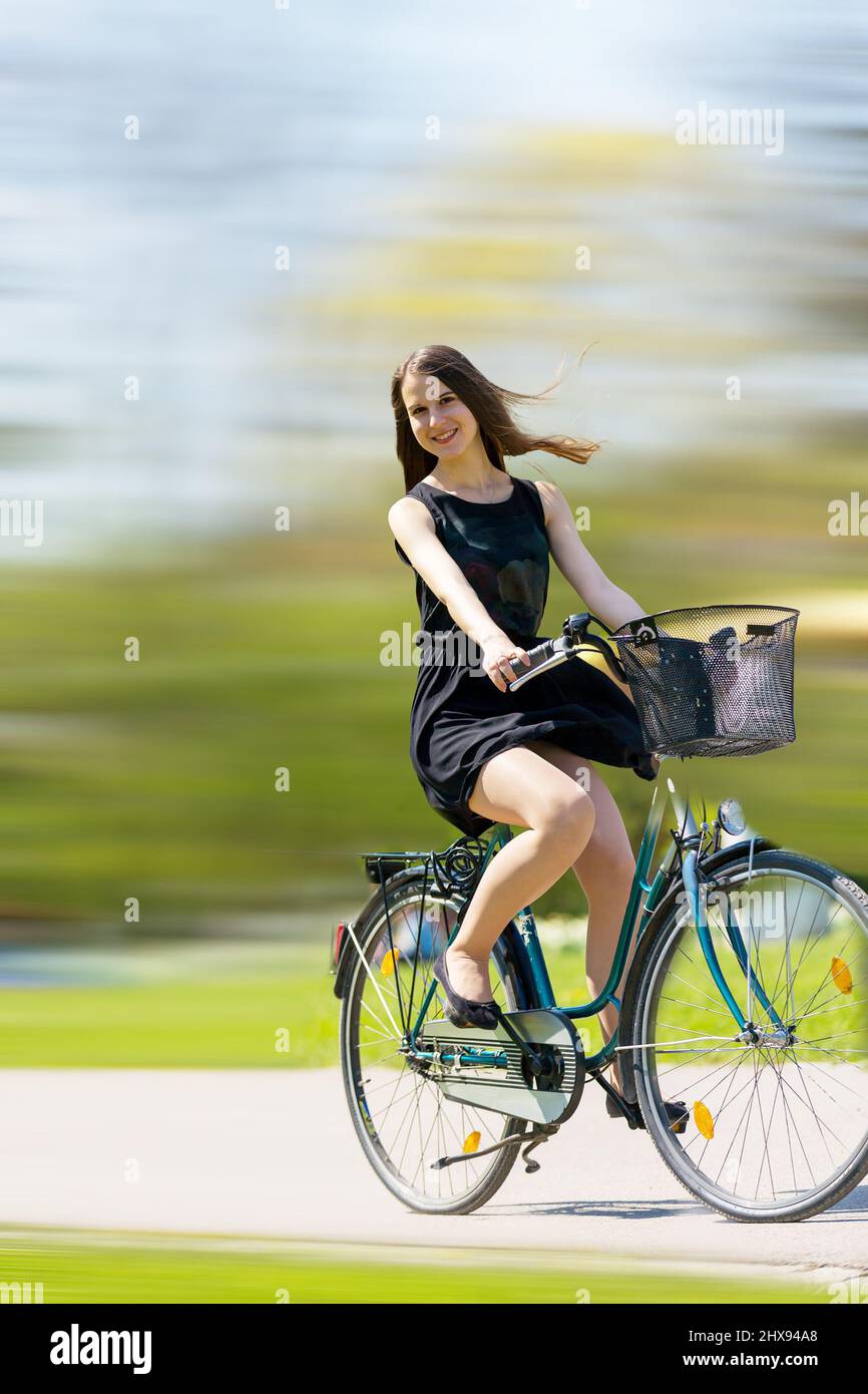 beautiful girl in a black short dress with long hair rides a bike in a ...