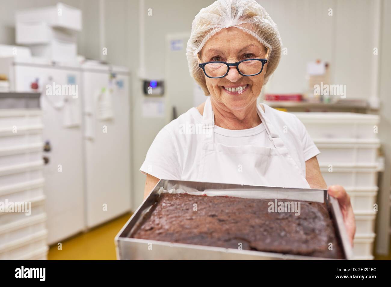 Older woman baker with experience proudly shows a fresh chocolate cake ...