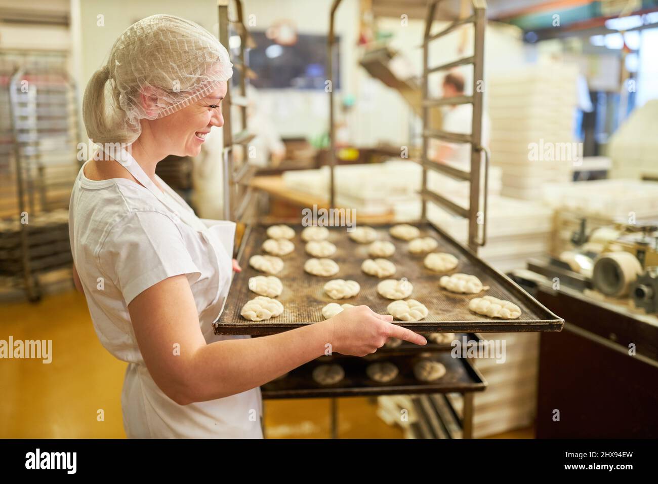 Young woman apprentice baker standing in front of yeast braids on ...
