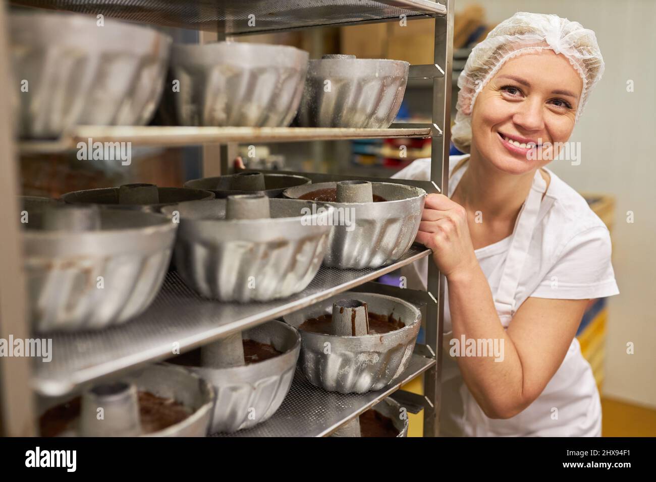 Young woman as a baker's apprentice pushes shelf trolley with Gugelhupf ...
