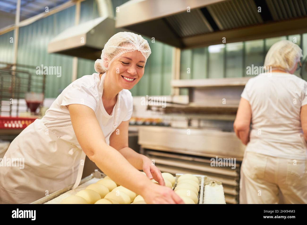 Happy young woman as a baker apprentice baking buns in a big bakery ...