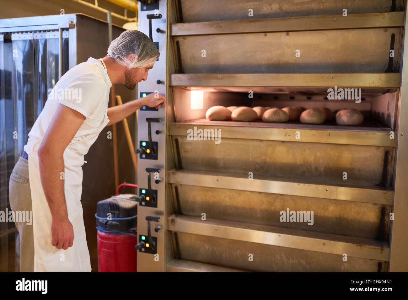 Young baker checking oven with loaves of bread in bakery or bakery ...