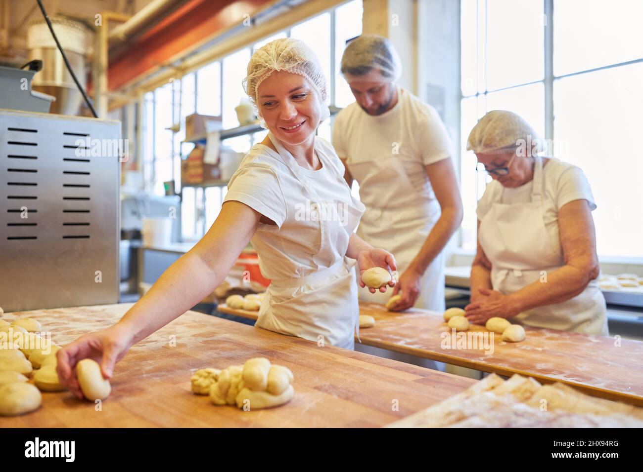 Three bakers bake small buns together in a large bakery Stock Photo - Alamy