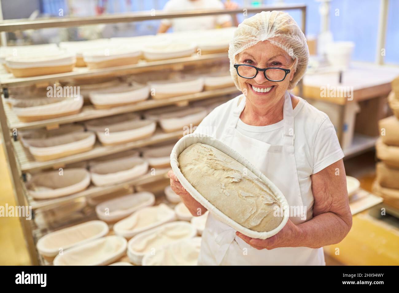 Senior woman baker with experience proudly shows a loaf of bread before ...