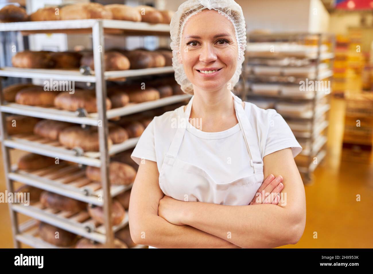 Young woman apprentice baker in a large bakery with her arms crossed ...