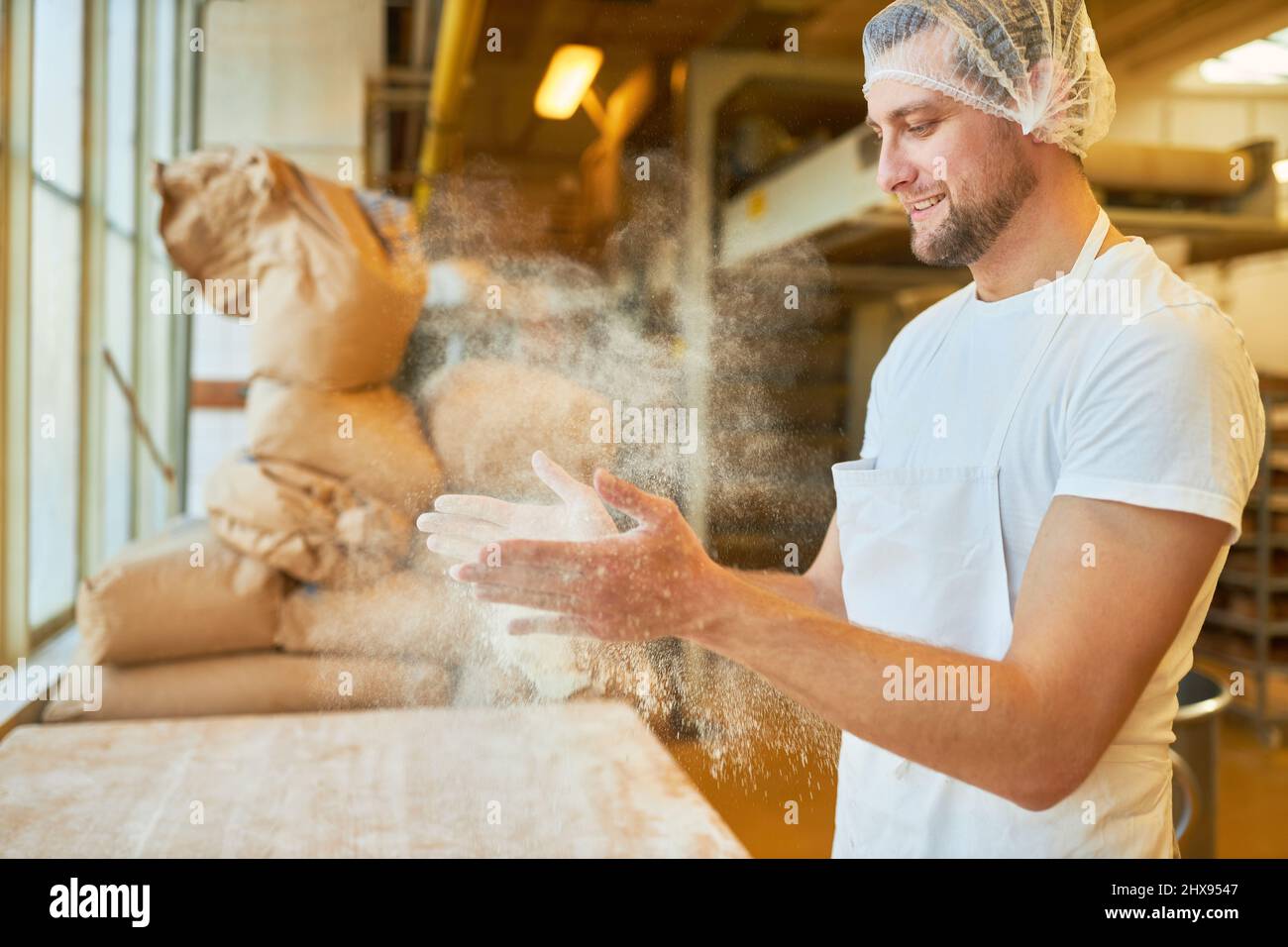 Young man as a baker apprentice smacks flour from hands while kneading ...